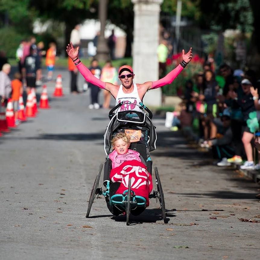 Runner with a child in a racing wheelchair celebrating during a race ...